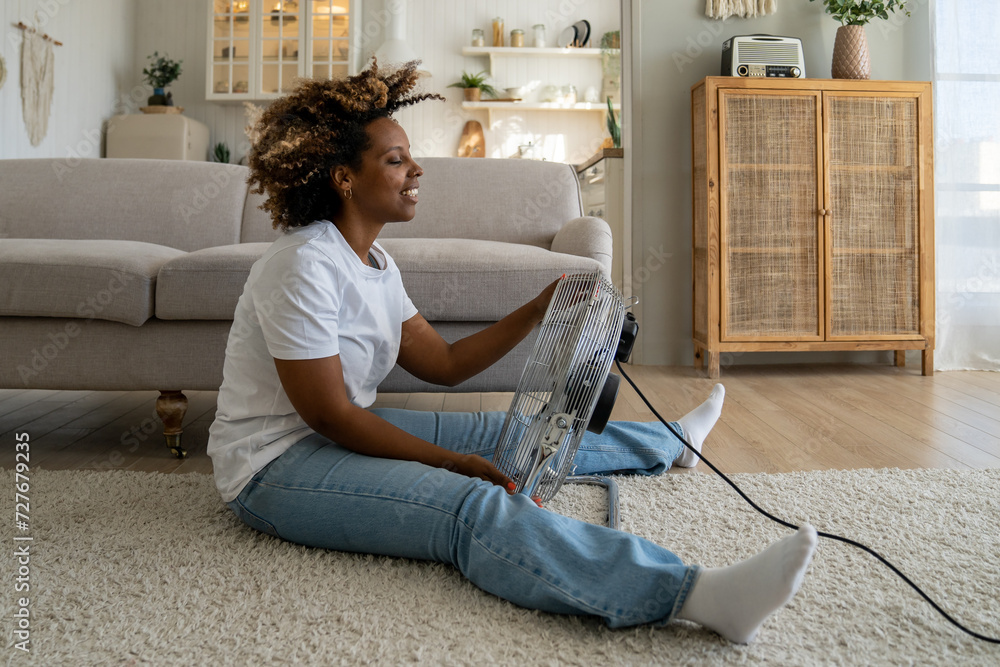 Overheating in homes. Happy young African American woman sits in front ...