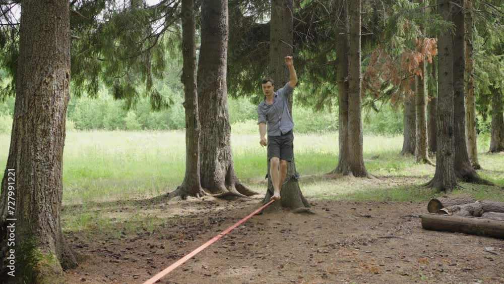Vidéo Stock Concentrated man balancing on a slackline between trees in ...