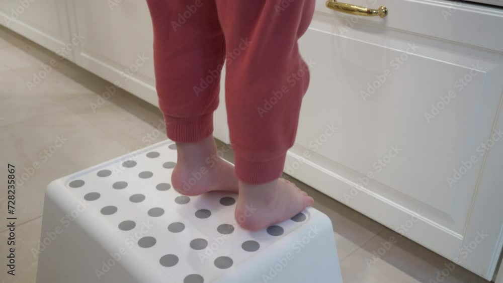 child little boy standing on tiptoes on a stool in the kitchen. 3-year ...