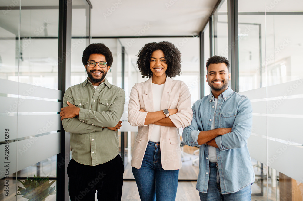 Three vibrant colleagues stand together in an office, their arms ...