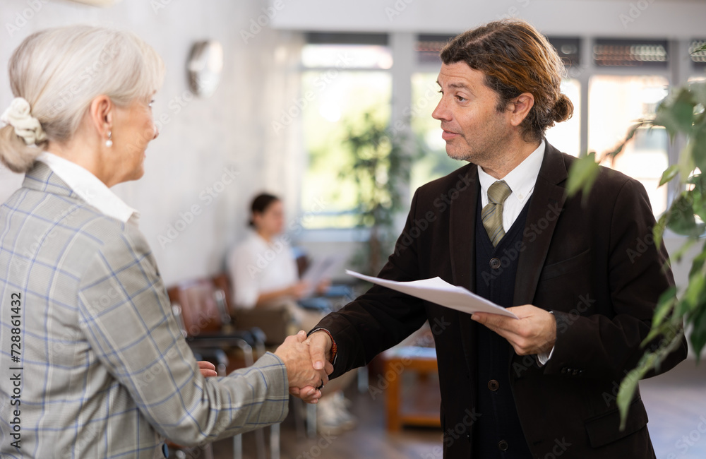 Mature woman shaking hands with male colleague after making changes to ...