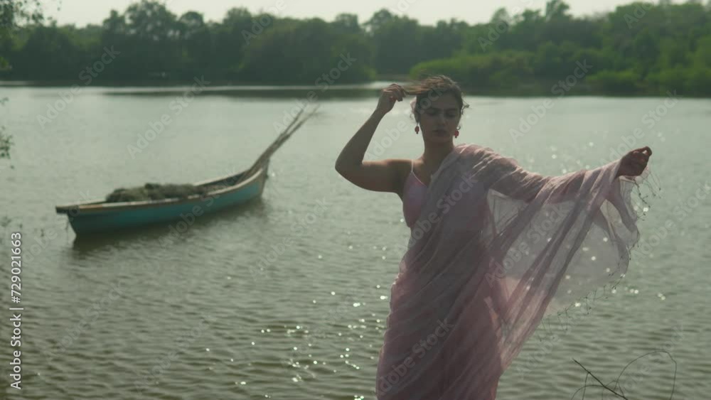 Vidéo Stock Woman in pink saree by the river, adjusting her attire ...