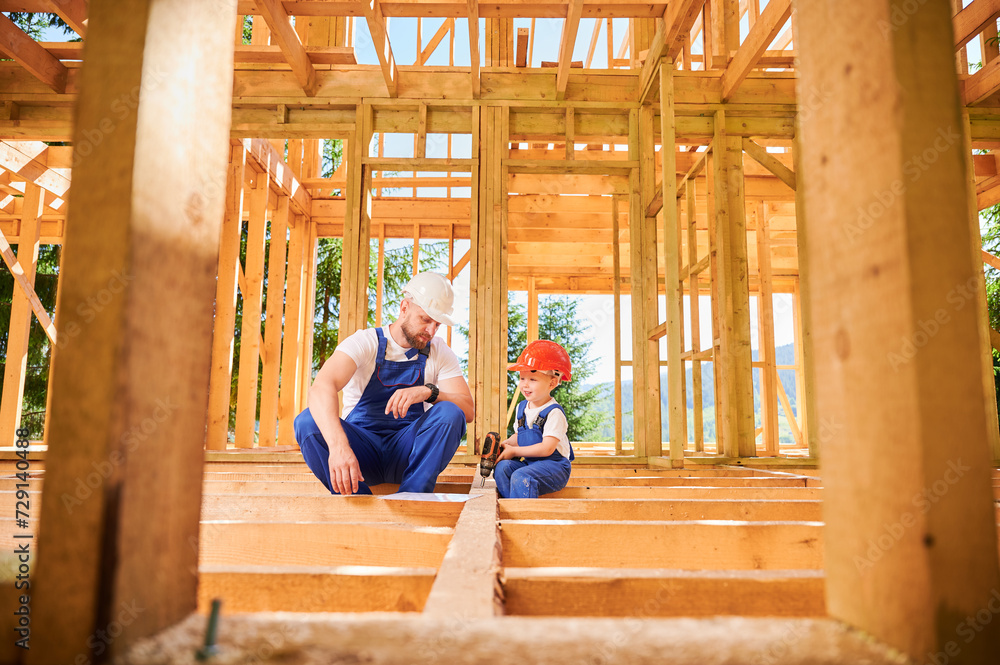 Father with toddler son building wooden frame house. Worker teaching ...