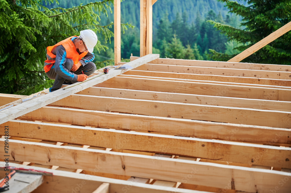 Carpenter in the process of building wooden frame house. Man measures ...