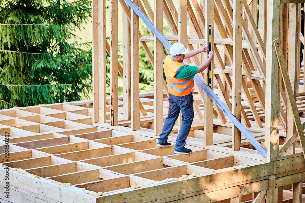 Carpenter constructing two-storey wooden frame house. Back view of man ...