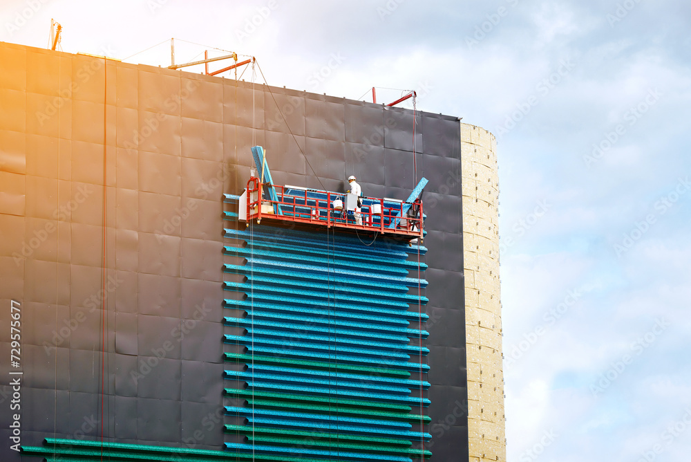 Worker on aerial platform, cladding wall with corrugated sheets. Worker ...