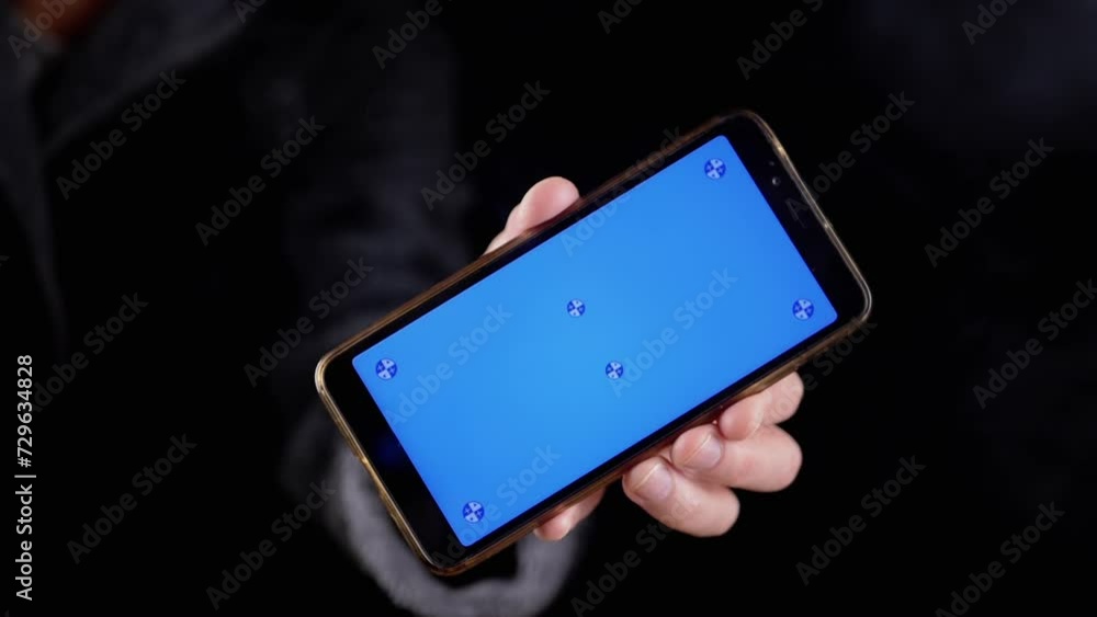 Hand Holding a Mobile Phone with a Blue Screen on a Black Background in ...