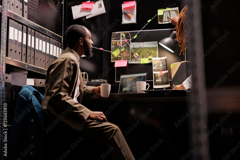Detective partners analyzing crime scene photos on evidence board and ...