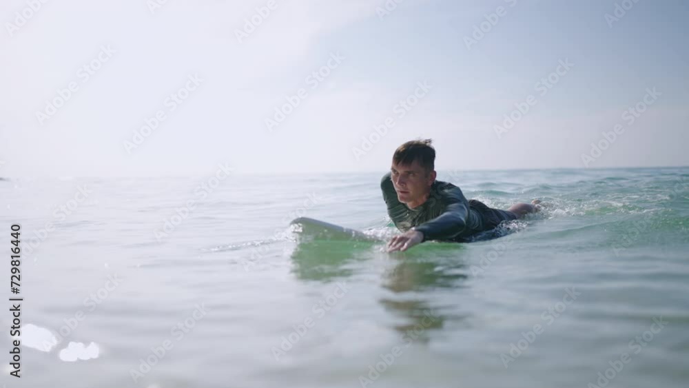 Male surfer in long sleeve rash guard paddling on surfboard. Man in ...