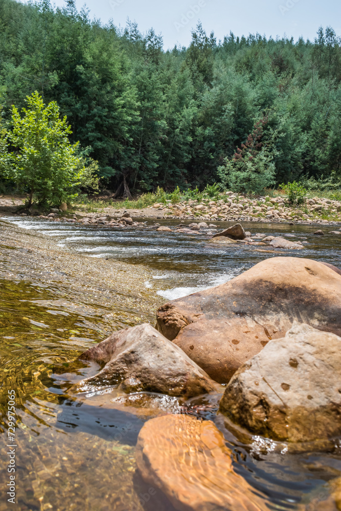 Water of the Ceira river flowing next to rocks and small weir with ...