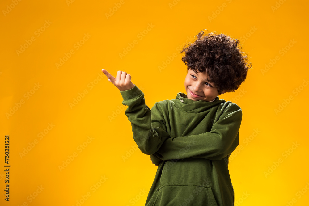 Thoughtful child boy pointing to an empty place on yellow background ...