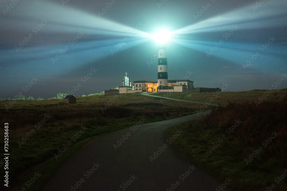 Phare qui eclaire en pleine nuit sur l'île d'Ouessant, face a la route ...
