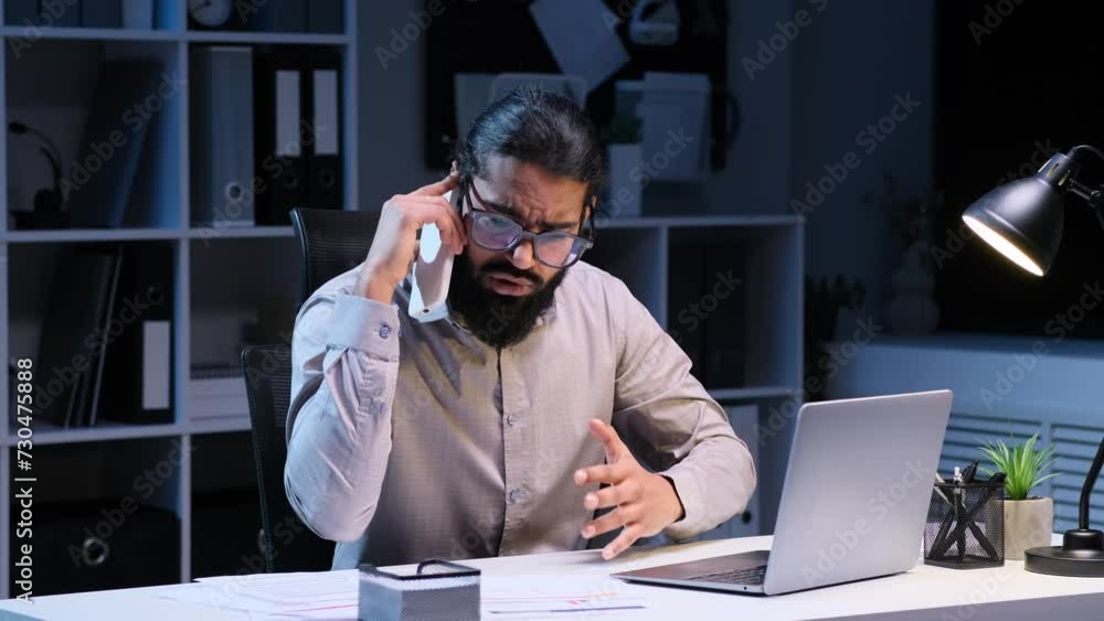 Upset and serious Indian manager talking on the phone while working in ...