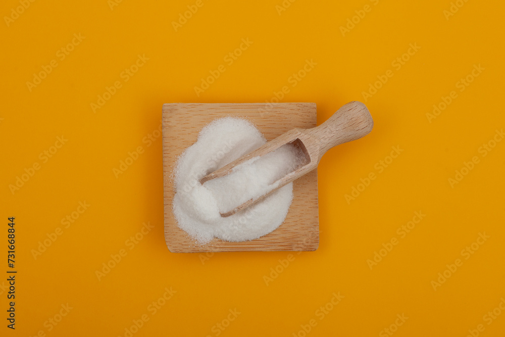 Food additive E316 in measuring scoop on yellow background. Sodium ...