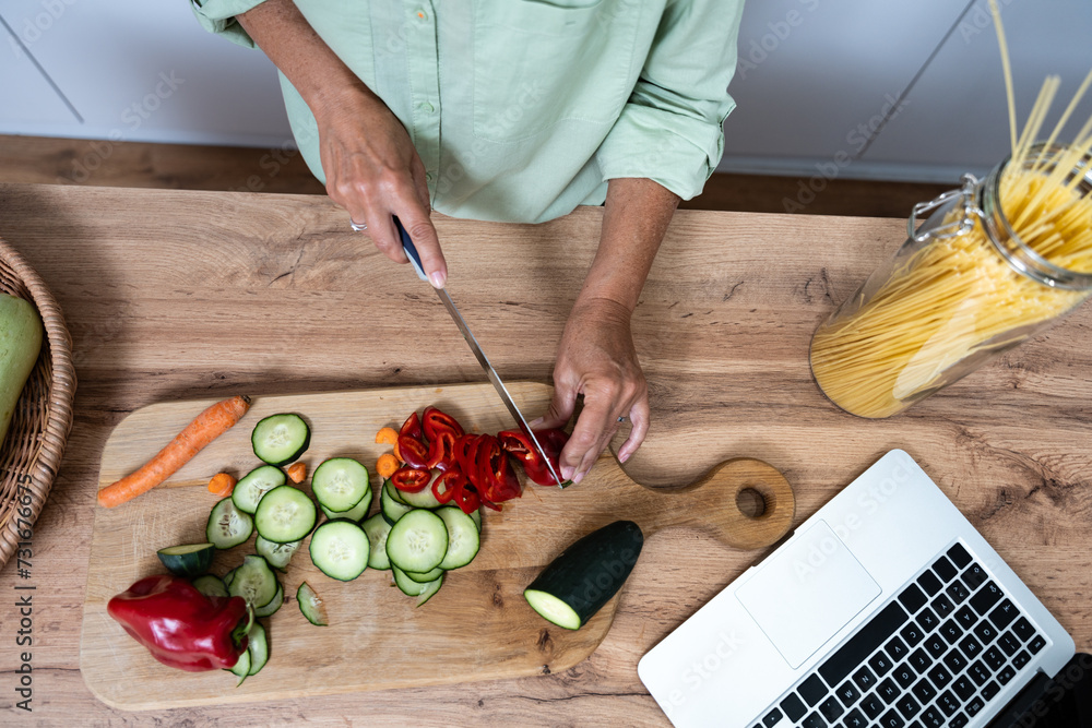 Senior woman cancer survivor reading recipes in kitchen from laptop ...