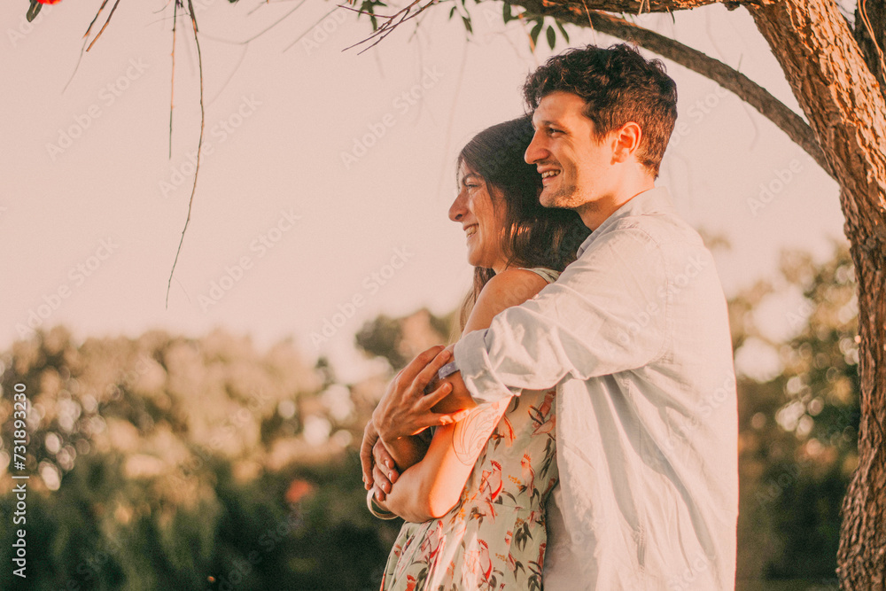 Happy, smiling couple in a green park with the sunset light, hugging ...