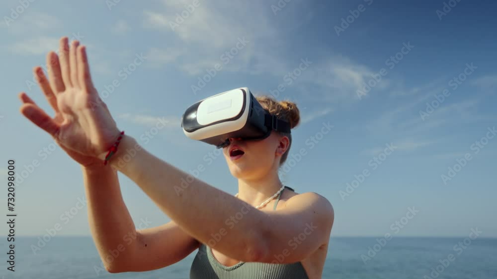 Woman in VR headset explores virtual beach scene, gesturing with hands ...