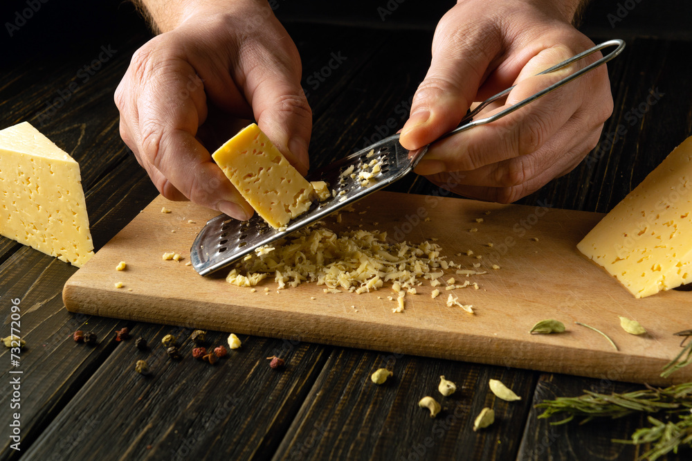 Grating hard cheese with a grater in a chef hand for preparing lunch on ...