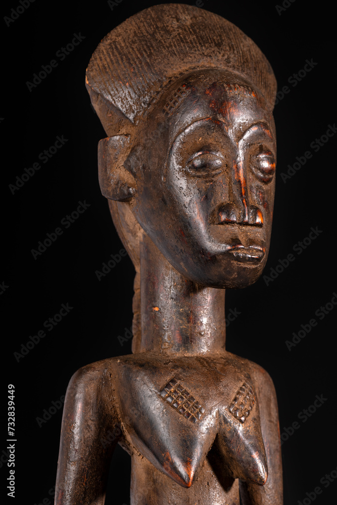Close-up of an African female figure carved in wood isolated on black ...