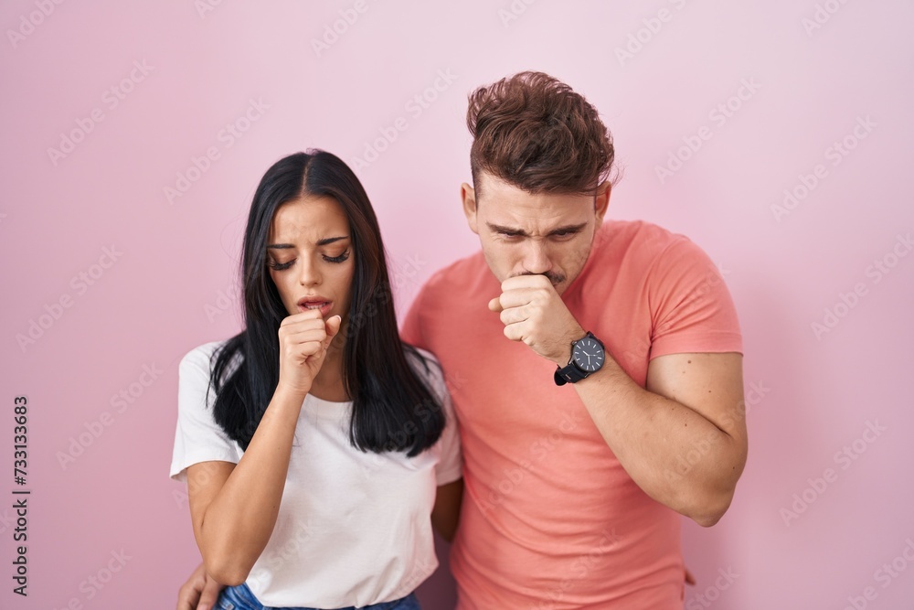 Young hispanic couple standing over pink background feeling unwell and ...
