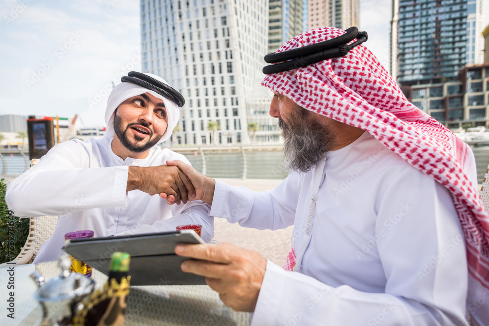 Arab businessmen wearing traditional emirati kandora meeting outdoors ...