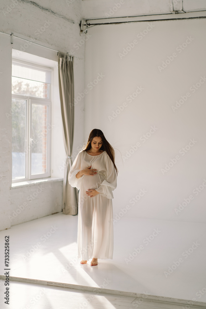 Cute young Pregnant girl sitting on the white studio in warm light with ...