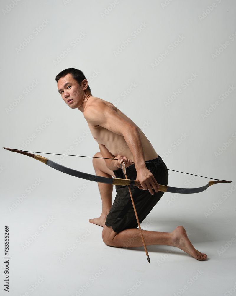 Full length portrait of fit asian male model, Holding hunting bow and ...