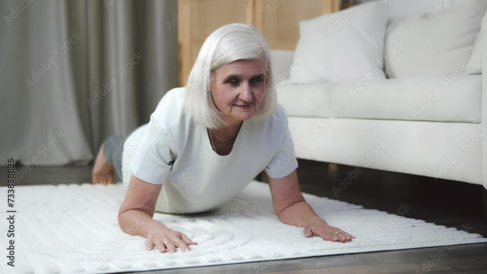 Cheerful active mature lady is training her upper body, doing push-ups ...