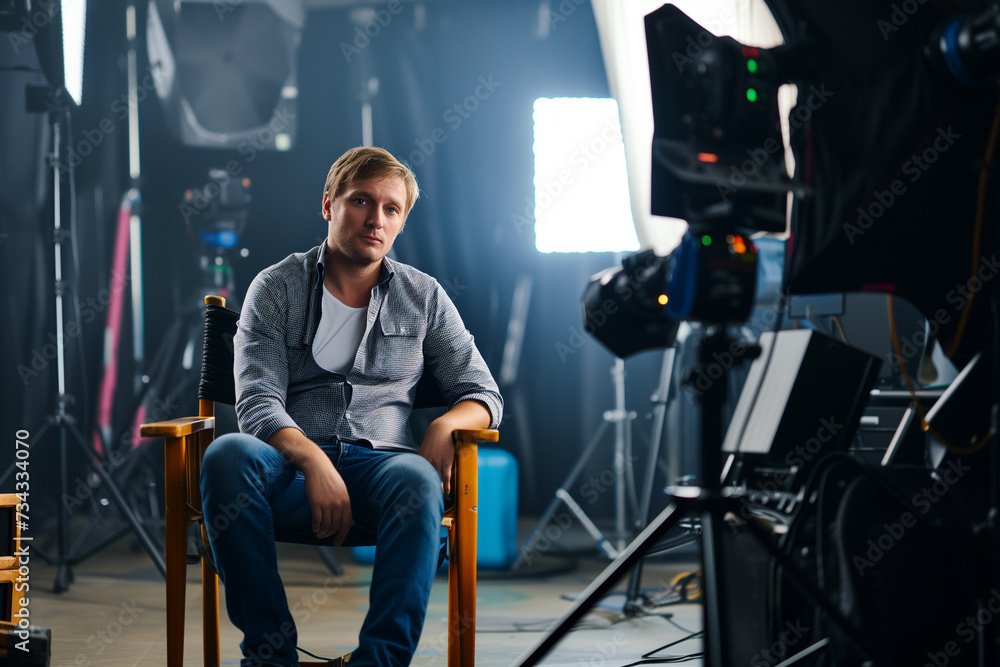 Film director sitting in a chair on the film set, man on a television ...