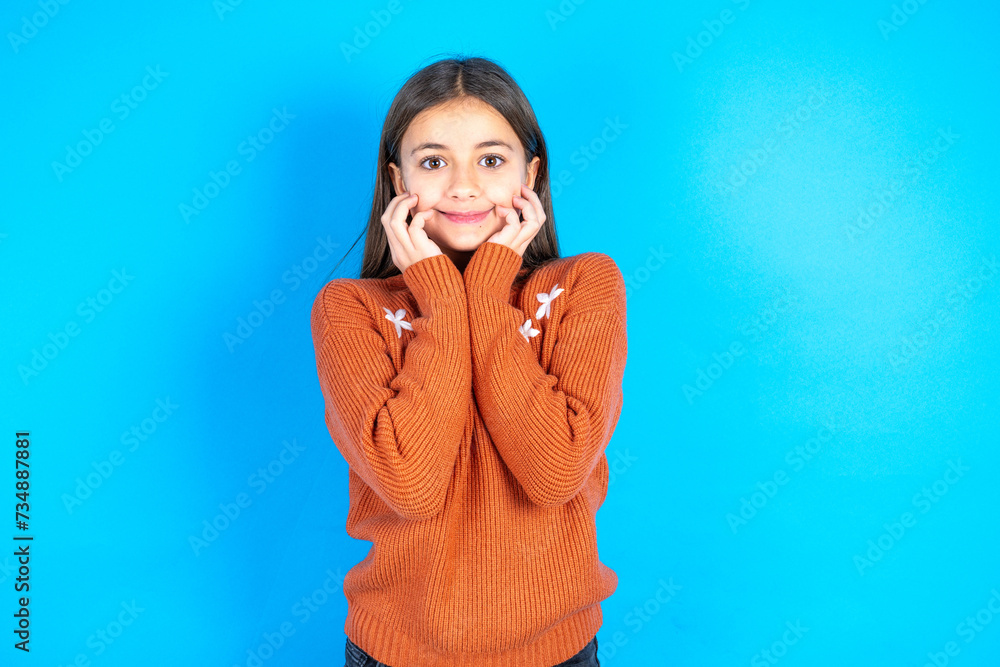 Speechless beautiful kid girl wearing orange sweater keeps hands near ...