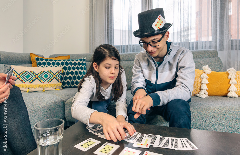 Siblings concentrate on a card game on the living room table, with a ...