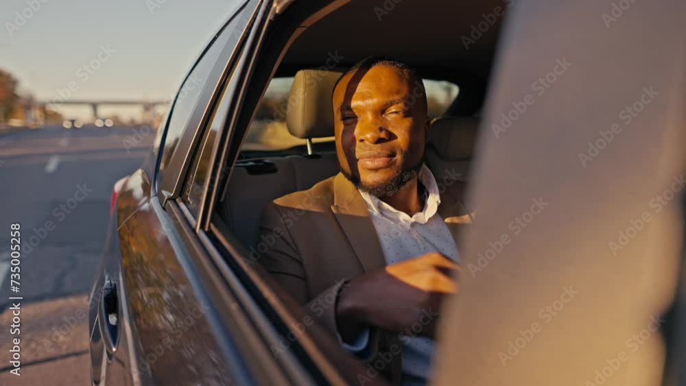 A confident man with Black skin opens the rear window in a modern car ...