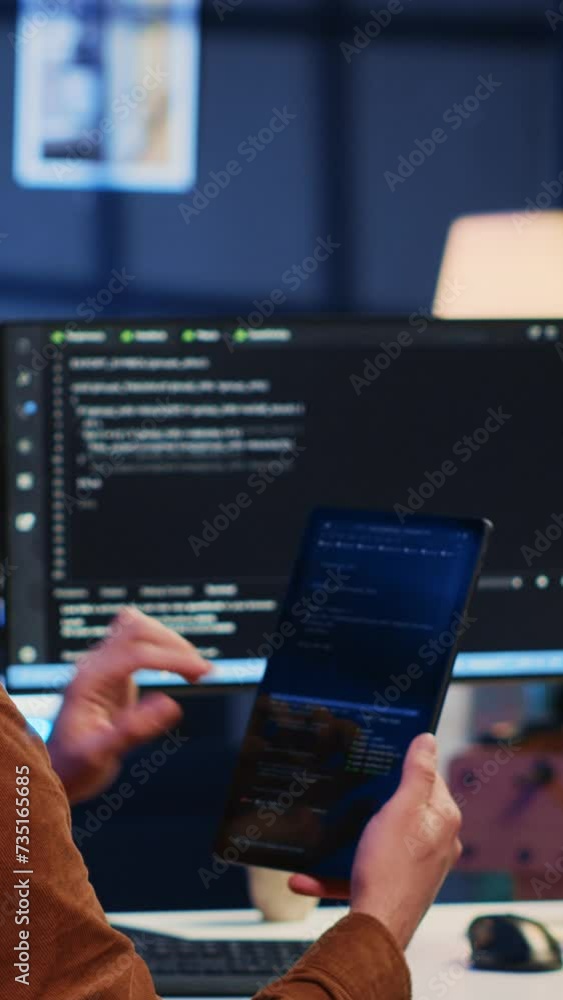 Software developer programming in home office, crosschecking lines of code between tablet and PC ...