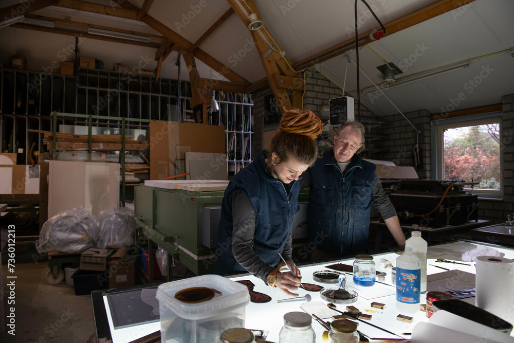 Apprentice female stained glass worker being taught lessons from ...