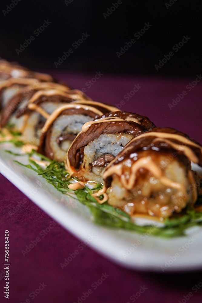 Beef teriyaki roll served on a black wooden plate, avocado, cucumber ...