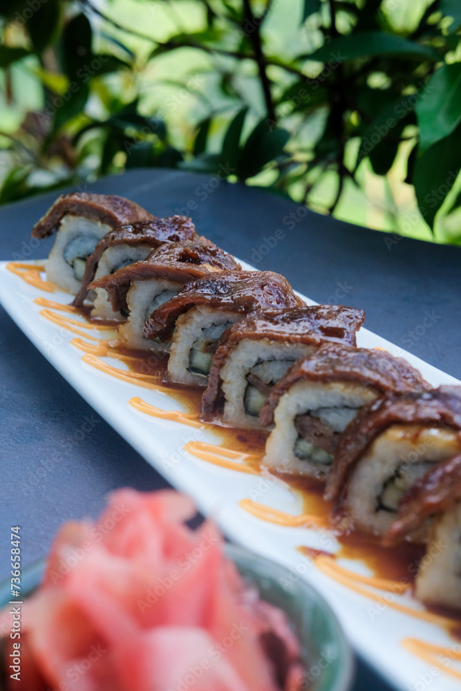 Beef teriyaki roll served on a black wooden plate, avocado, cucumber ...