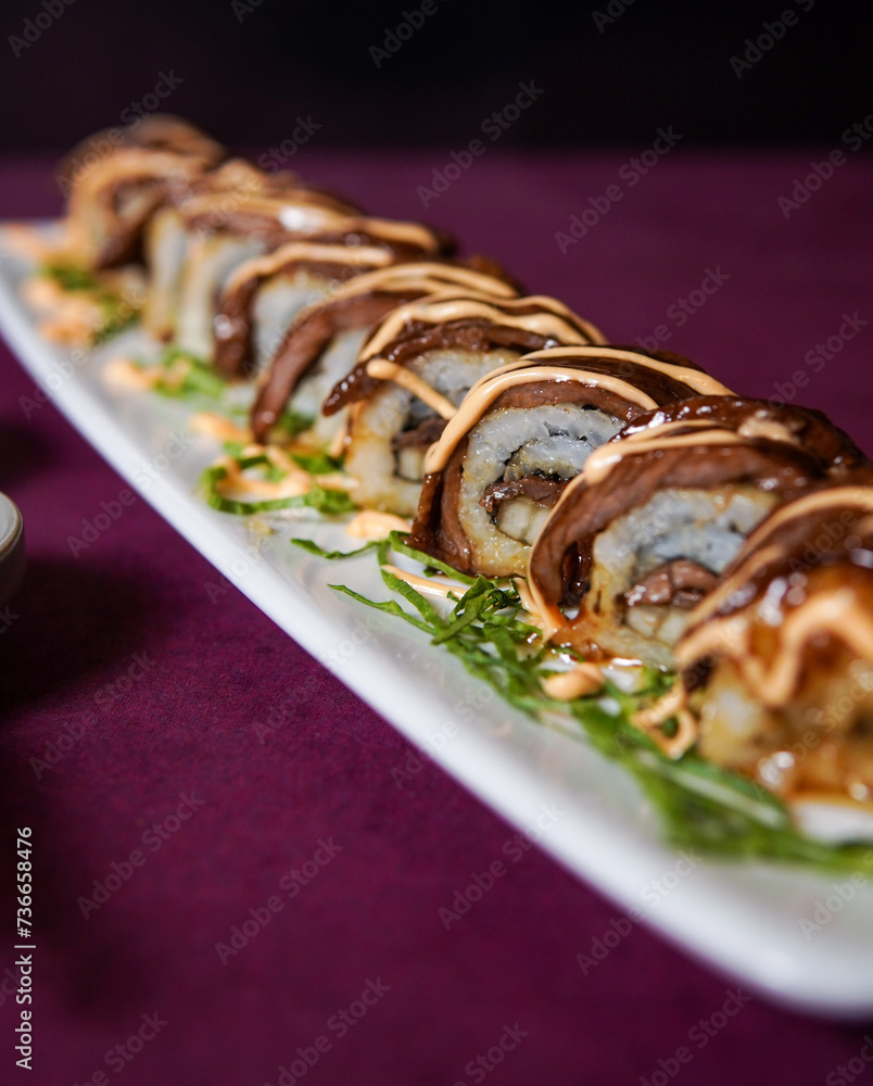 Beef teriyaki roll served on a black wooden plate, avocado, cucumber ...