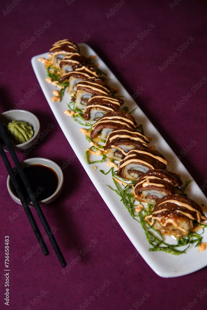 Beef teriyaki roll served on a black wooden plate, avocado, cucumber ...