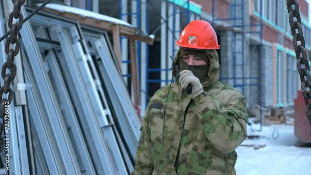 Worker using portable radio and hanging chains of crane on building ...