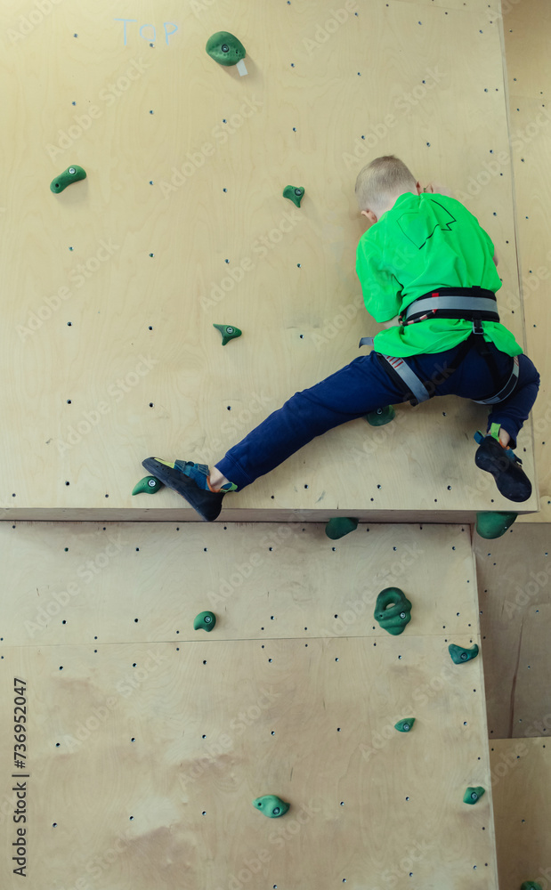 Rock climbing for children. Blond boy in a green shirt is climbing ...