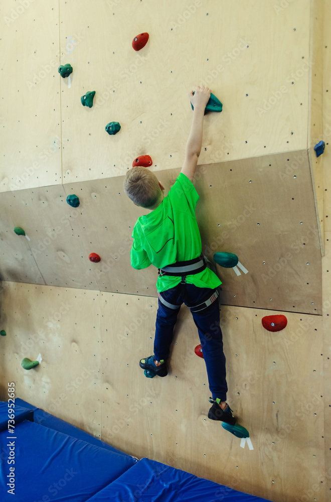 Rock climbing for children. Blond boy in a green shirt is climbing climbing wall. Bouldering ...