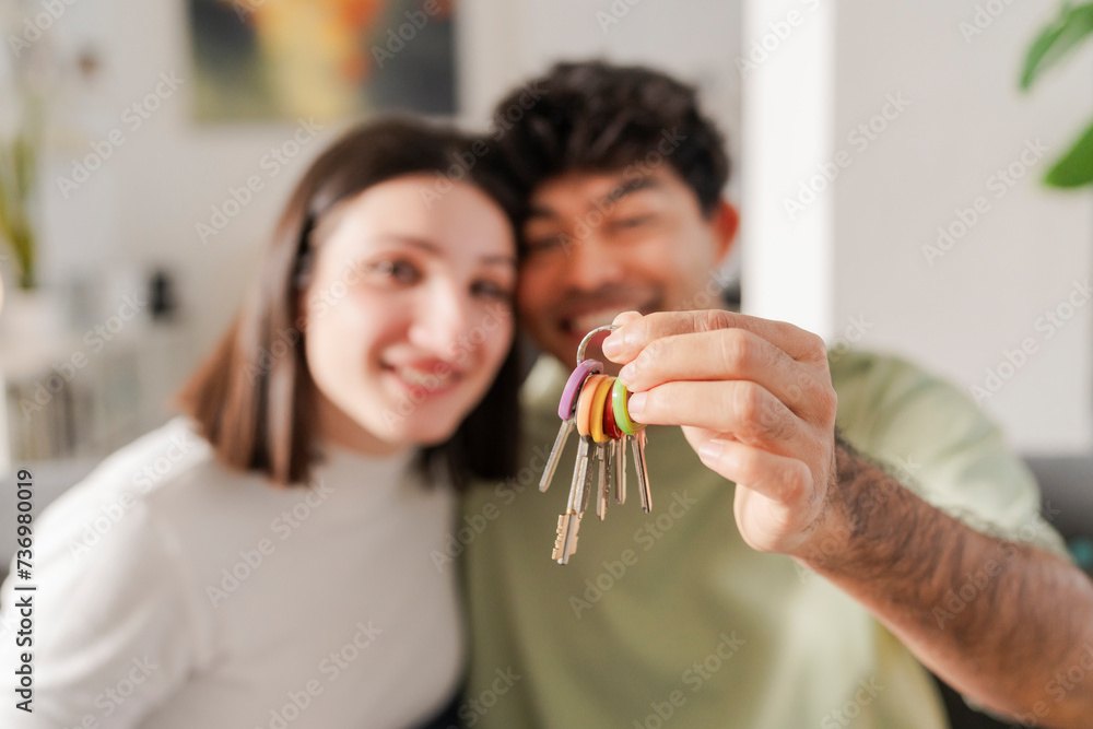 Ecstatic young couple smiling and holding up a set of new house keys ...