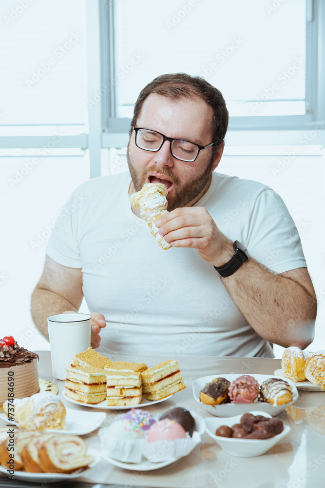 Man sitting in front of a table full of sweet food, eating pastry with ...