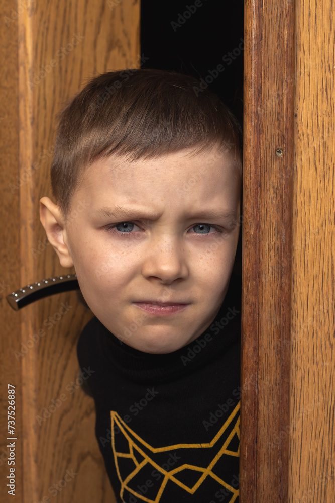 School boy opened the door to the house and looks out from under the ...