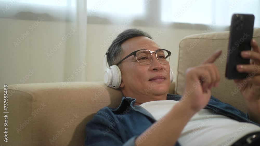 Asian senior man listen to music with headphone and relax on sofa at ...