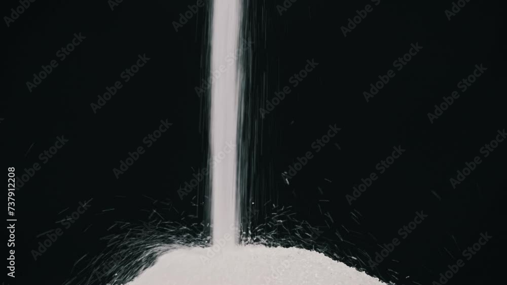 Sugar pours in stream on black background slow motion close-up. White ...