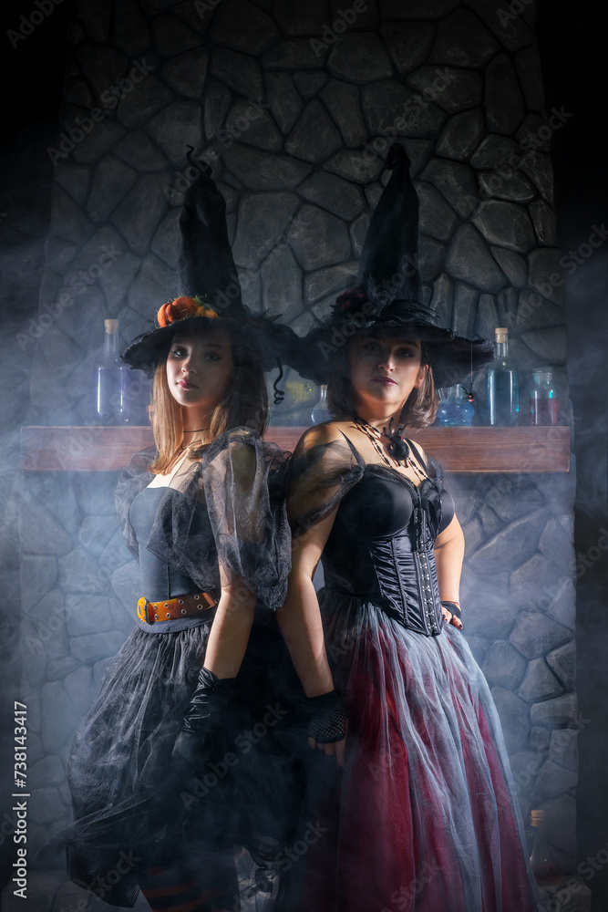 Halloween magic. Young girls in hats and witch costumes in a dark room ...