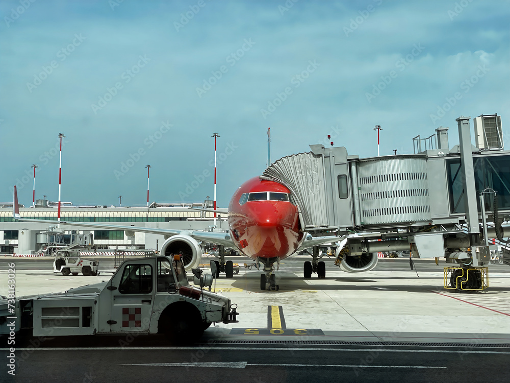 Passenger airplane with a red nose cone docked at the airport terminal ...
