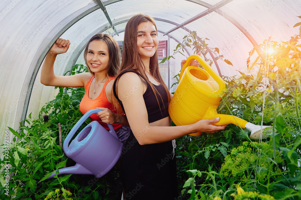 Two 26 year old women pose in greenhouse with garden watering cans in ...