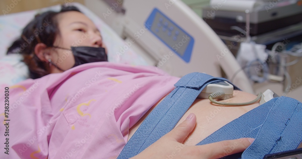 Pregnant woman lying in a hospital bed, fetal monitor strapped to her ...